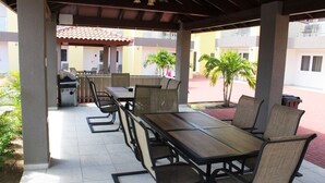 Um pátio externo com uma mesa de jantar comprida, cadeiras e área de churrasco.