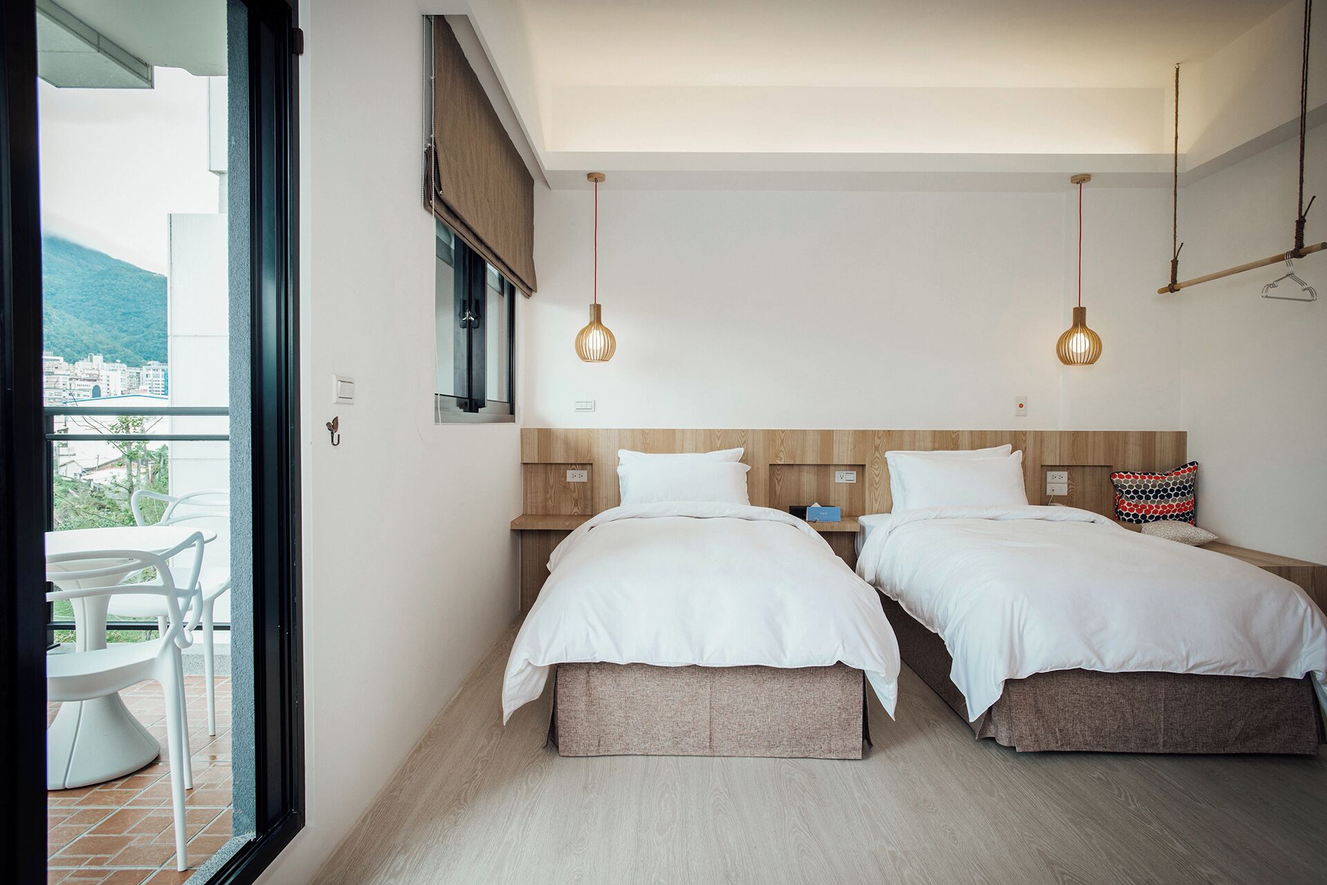 Quarto de hotel com duas camas, varanda com cadeiras e vista para a cidade.