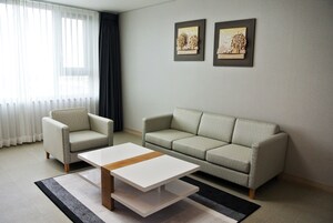 Uma sala de estar moderna com um sofá, poltrona e mesa de centro. Há duas obras de arte emolduradas na parede.
