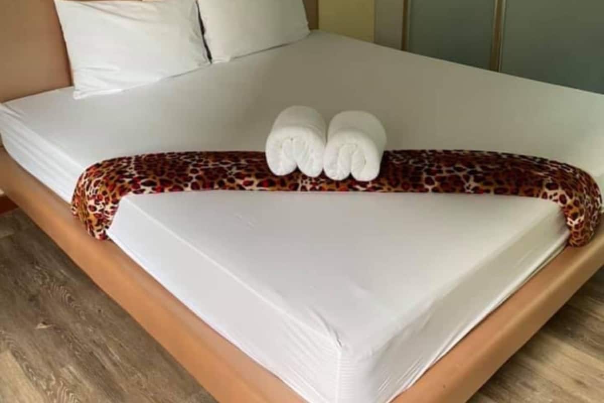 Uma cama bem arrumada com lençóis brancos, duas almofadas e um cobertor estampado com padrão de leopardo.