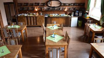 Uma área de refeições com mesas e cadeiras de madeira, uma cozinha com máquinas de costura antigas e um relógio na parede.