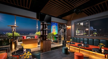 Um bar no terraço com vista para a cidade, mesas e cadeiras, e um letreiro luminoso.