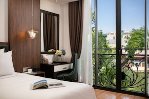 Quarto de hotel com uma cama, uma escrivaninha com cadeira, mesa de cabeceira, abajur e vista exterior por uma grande janela.