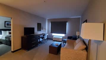 Quarto de hotel com cama, televisão, escrivaninha, sofá e janela.