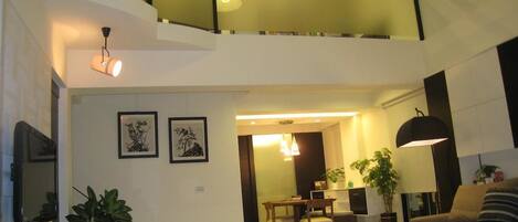 Uma sala de estar moderna com teto alto, área de refeições e escada que leva a um andar superior.
