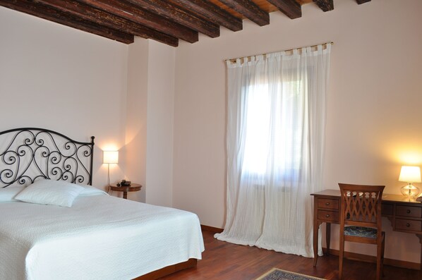Quarto com cama, mesa de cabeceira, cadeira e janela com cortinas.