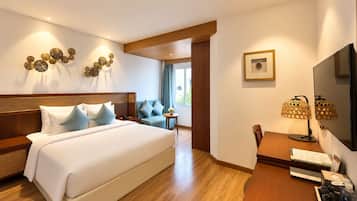 Quarto de hotel com uma cama grande, uma escrivaninha com luminária e uma televisão.