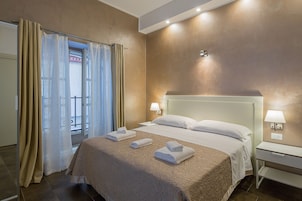 Quarto de hotel com uma cama grande, duas mesas de cabeceira e vista para o exterior através de uma janela com cortinas.