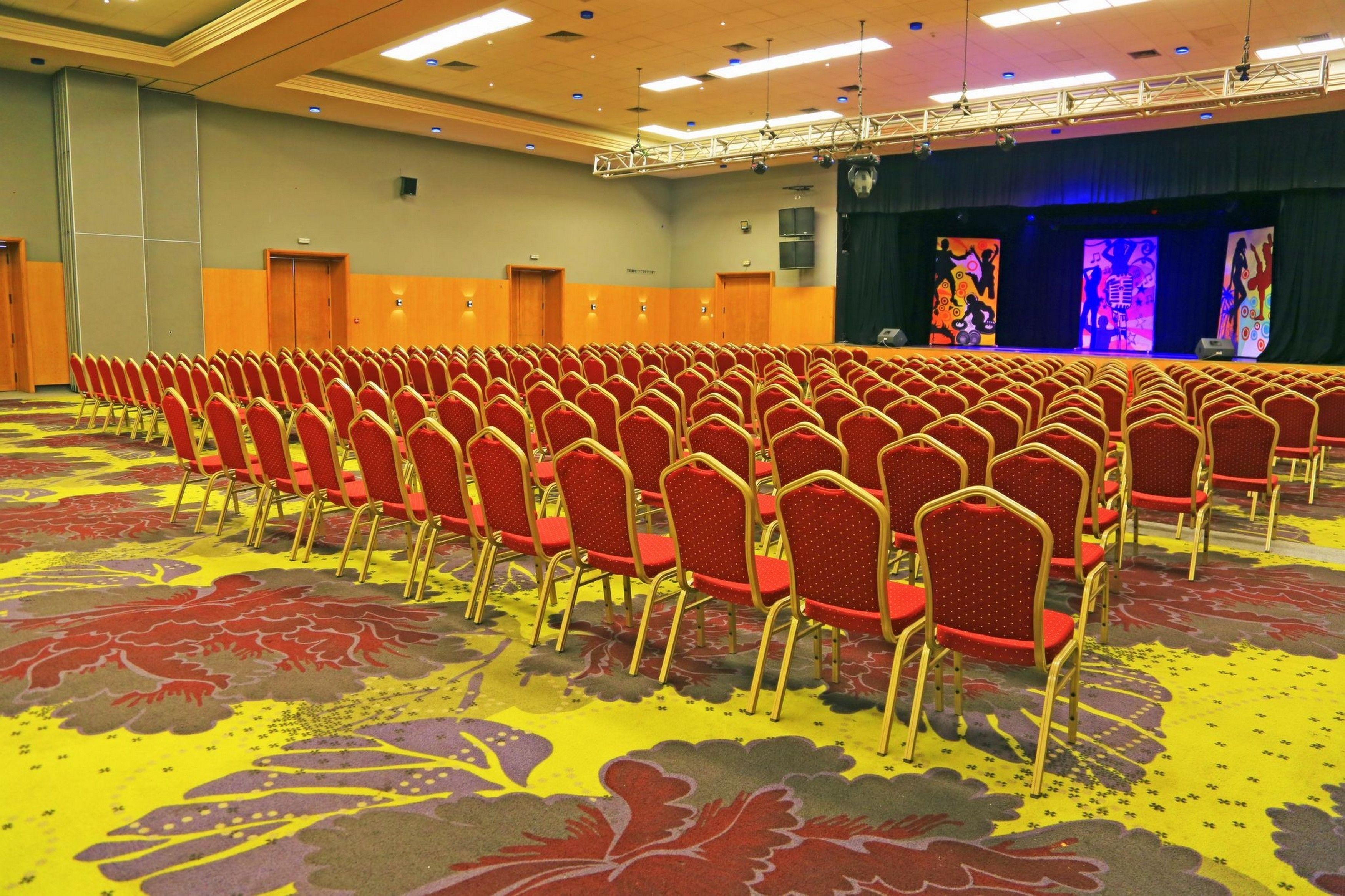 Uma sala de conferência com fileiras de cadeiras vermelhas e um palco com um fundo.