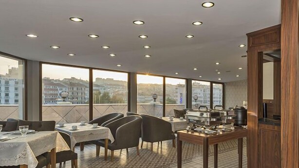 Restaurante com mesas, cadeiras, serviço de buffet e amplas janelas com vista para a cidade.
