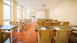Uma sala de conferências com mesas, cadeiras, tela de projeção e uma grande janela.