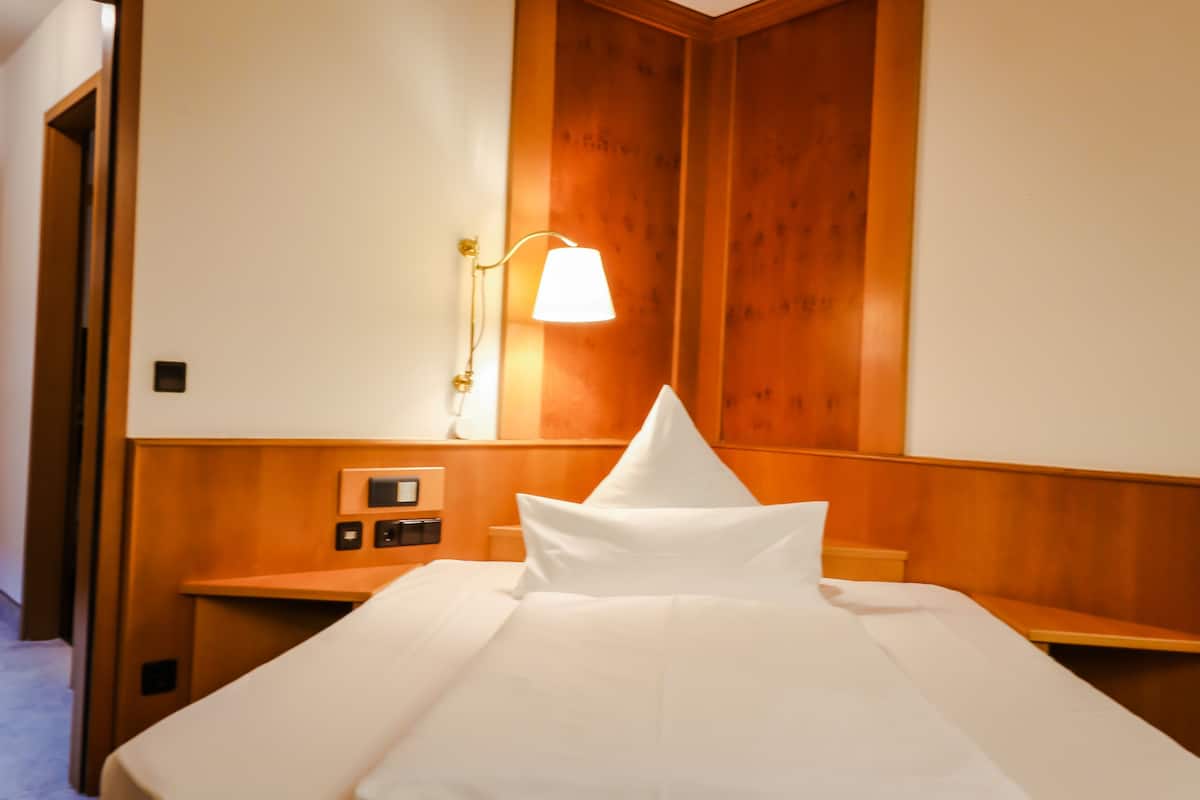 Quarto de hotel com cama, mesa de cabeceira, luminária e painéis de madeira nas paredes.
