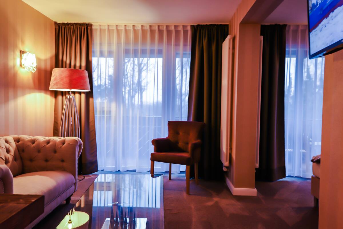 Quarto de hotel com sofá, poltrona e televisão de tela plana fixada na parede.