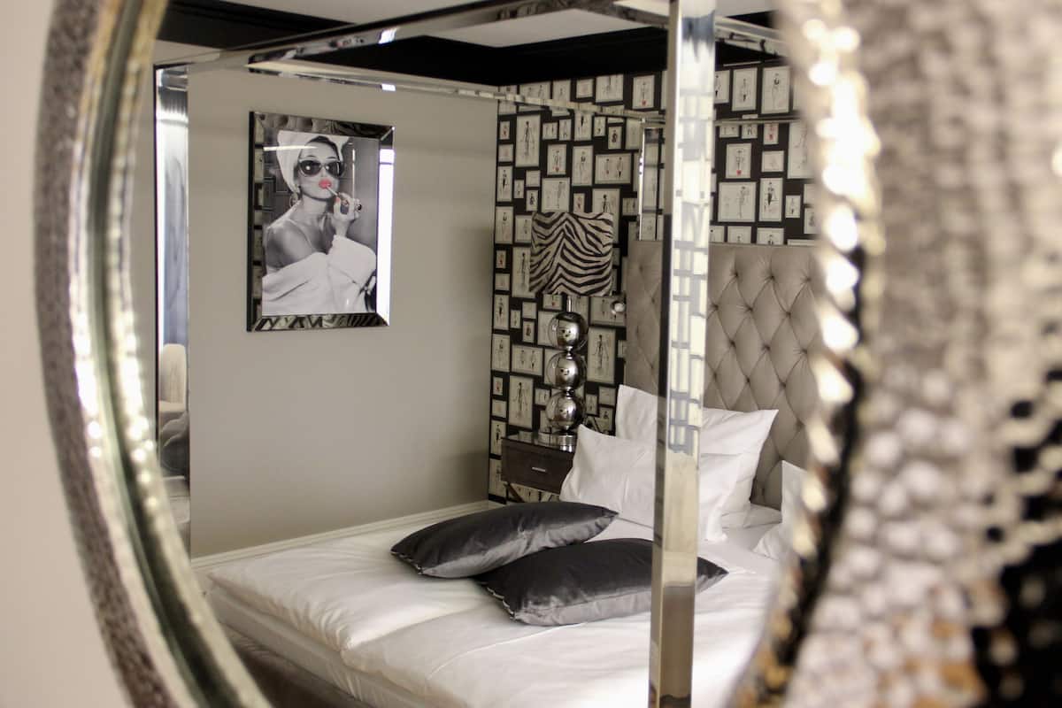 Quarto com cama, almofadas, espelho e parede decorada com quadros.
