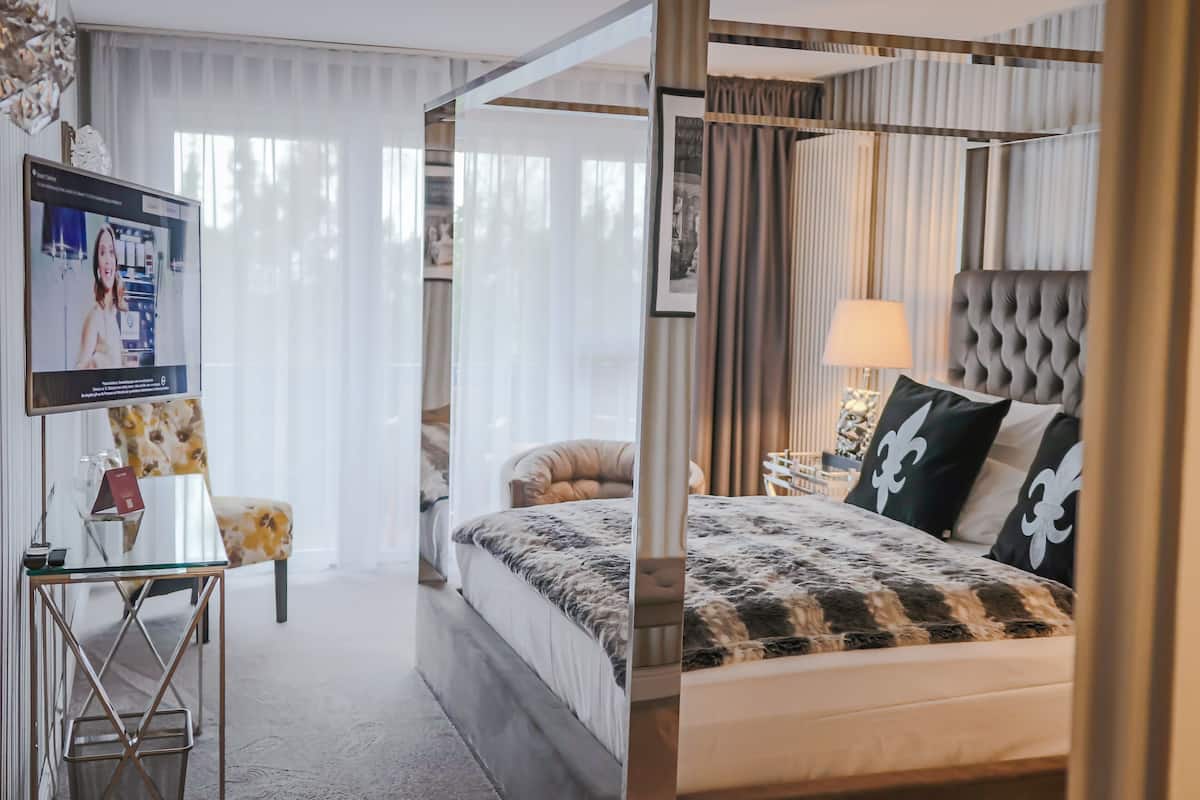 Quarto de hotel moderno com uma cama de dossel, uma escrivaninha de vidro e uma televisão exibindo um vídeo.