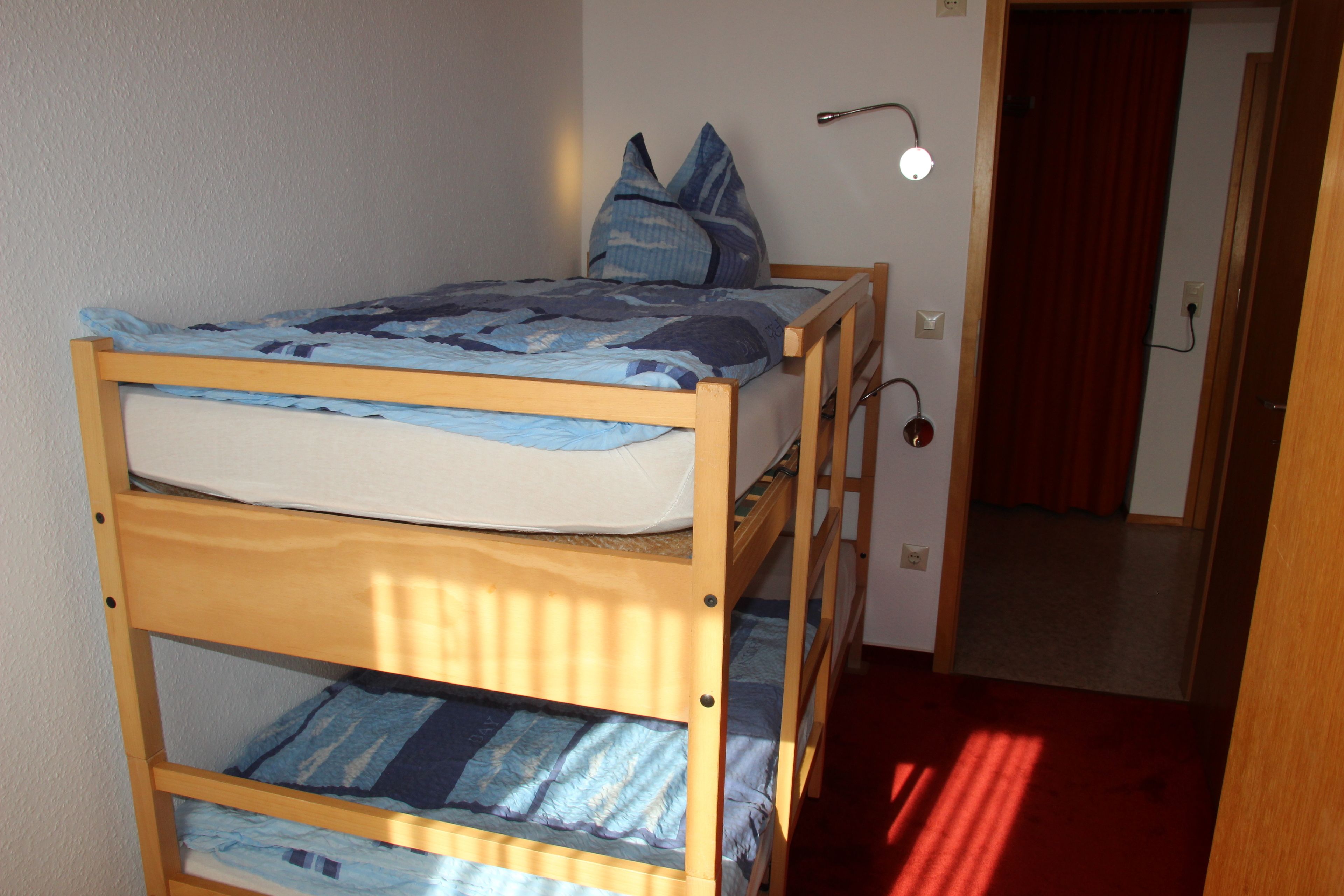Uma cama beliche com colcha estampada em azul e branco, cabeceira de madeira e abajur.