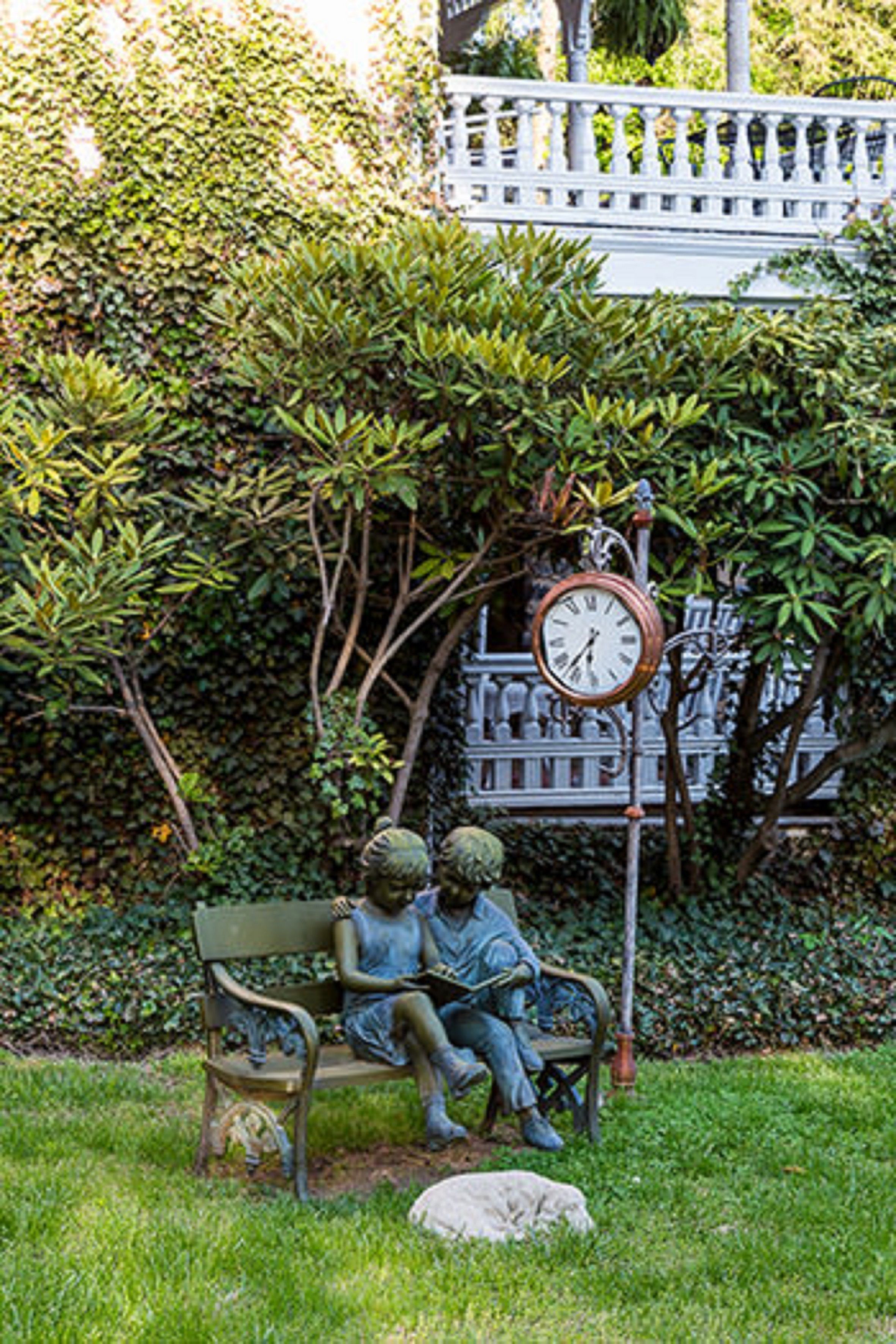Estátua de duas figuras sentadas num banco, com um relógio ao fundo.