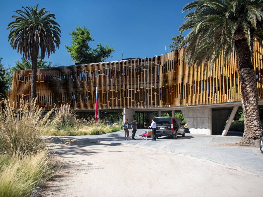 Um edifício moderno com fachada de madeira, área de estacionamento coberta e palmeiras.