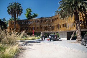 Um edifício moderno com fachada de madeira, área de estacionamento coberta e palmeiras.