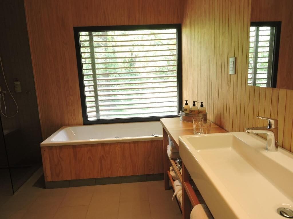Uma casa de banho moderna com toucador de madeira, banheira e uma grande janela com persianas.