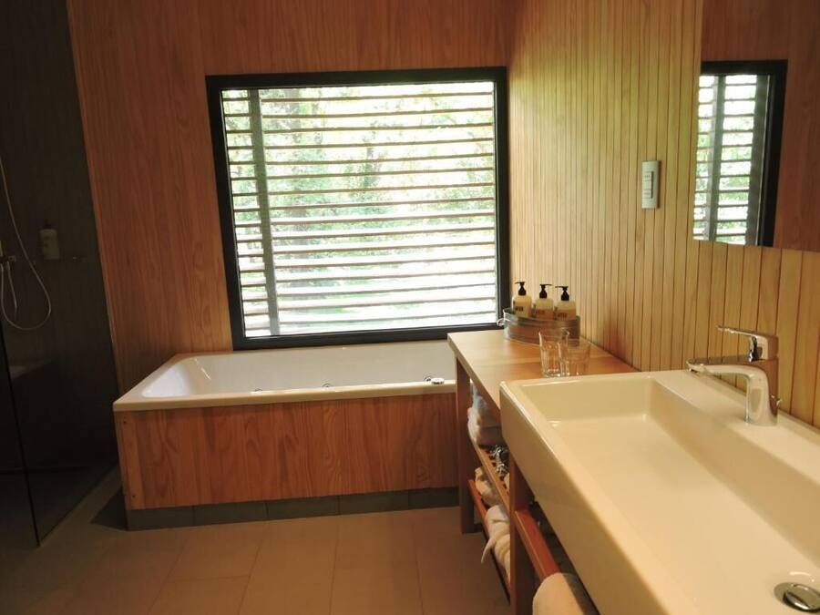 Uma casa de banho moderna com toucador de madeira, banheira e uma grande janela com persianas.