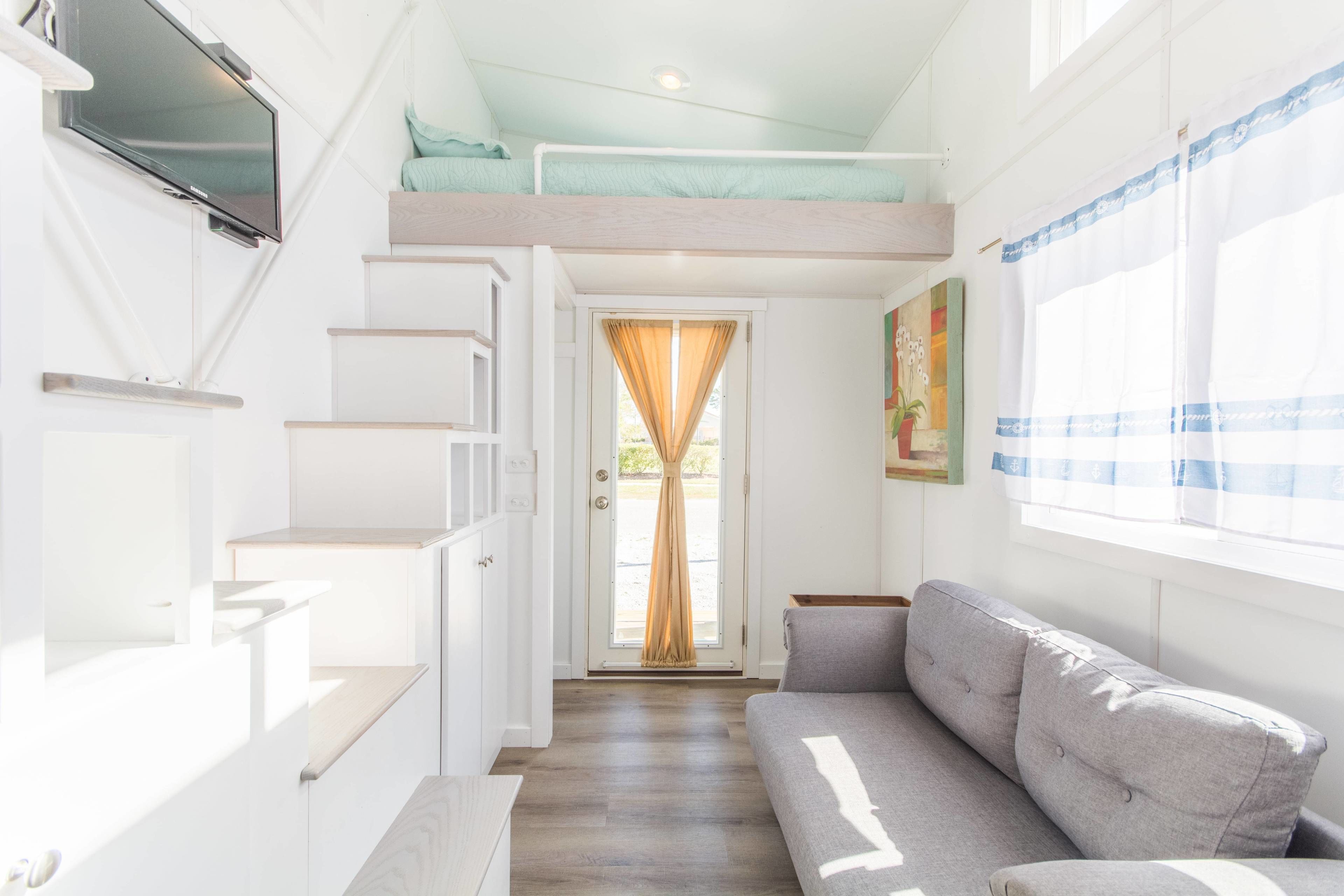 Quarto compacto com beliche, sofá, televisão e porta para o exterior.