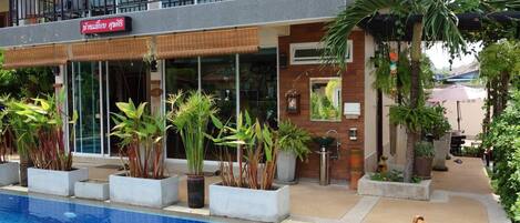 Um hotel com piscina, plantas em vasos e uma placa em idioma estrangeiro.