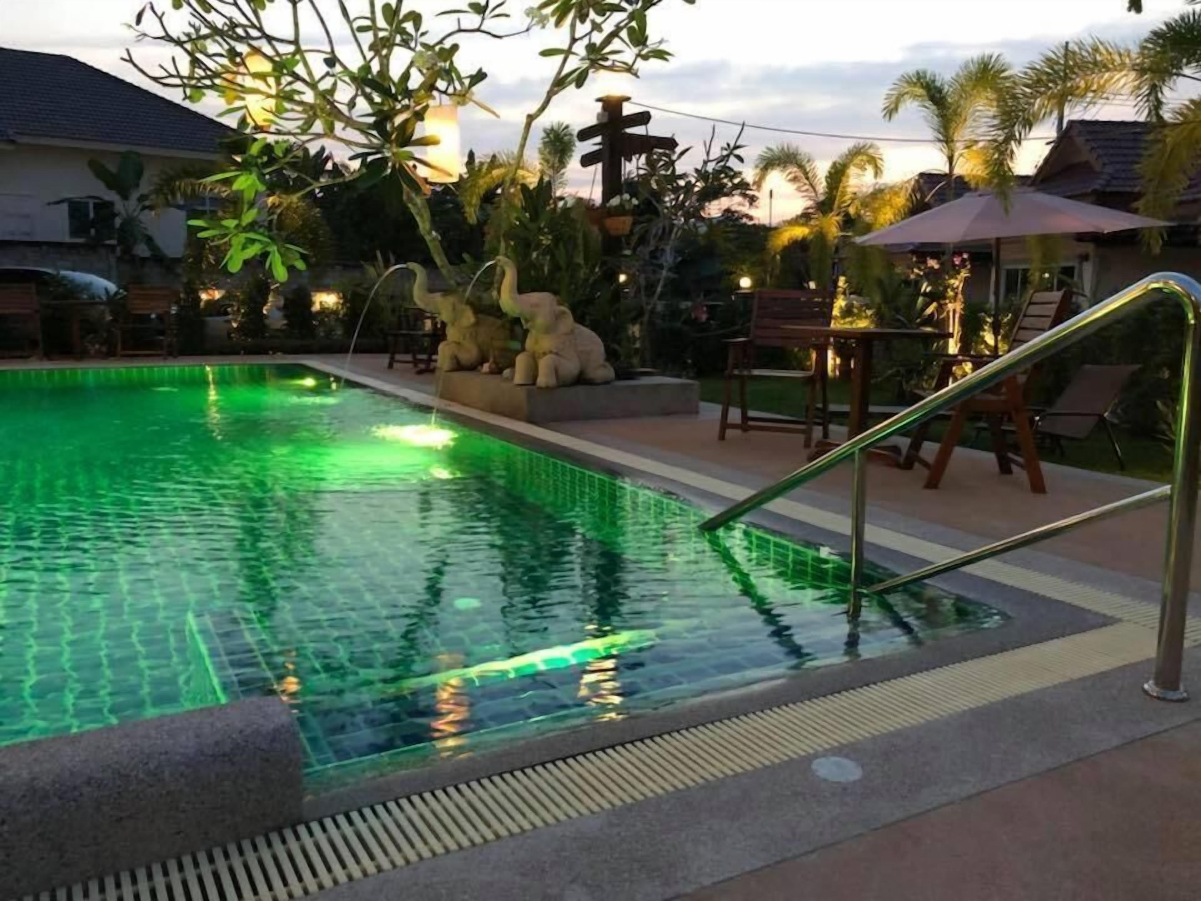 Piscina com um atrativo aquático iluminado em verde, rodeada por espreguiçadeiras e uma palmeira.