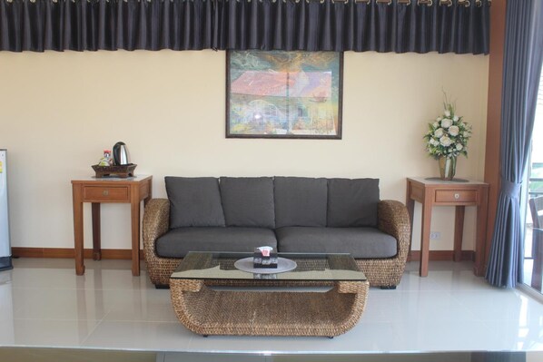 Uma sala de estar com sofá, mesa de centro, duas mesinhas laterais, um quadro na parede e um vaso com flores.