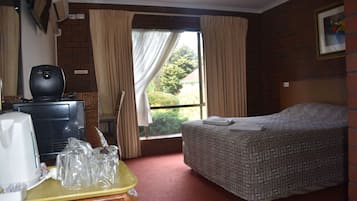 Quarto de hotel com cama, televisão, cafeteira e janela com cortinas.