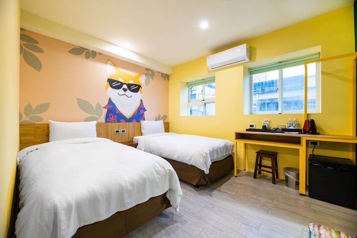 Quarto com duas camas, uma escrivaninha, uma cadeira, ar-condicionado e uma janela.