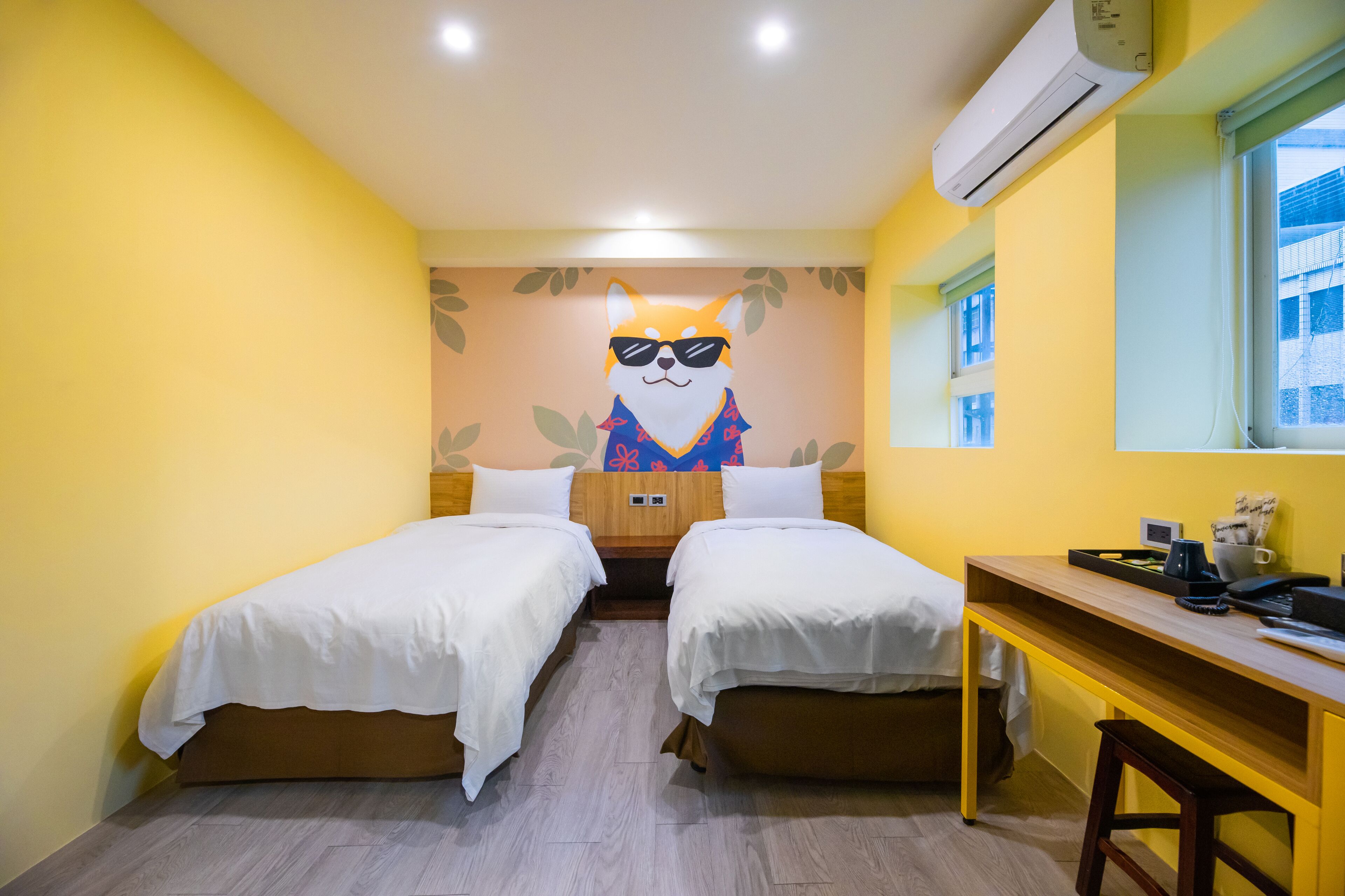 Quarto com duas camas, uma escrivaninha e um mural de gato na parede.