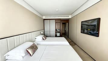 Quarto de hotel com duas camas, televisão, minibar e porta deslizante para uma casa de banho.