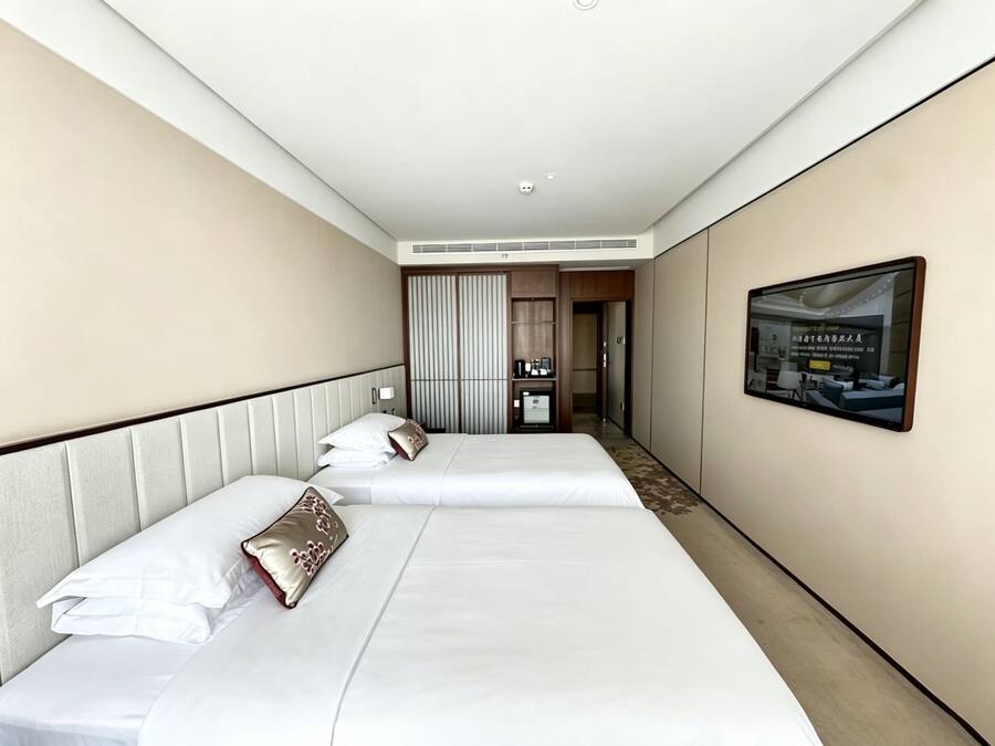 Quarto de hotel com duas camas, televisão, minibar e porta deslizante para uma casa de banho.