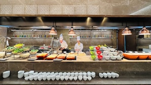 Uma cozinha industrial com chefs preparando alimentos, eletrodomésticos de aço inoxidável e ingredientes organizados.