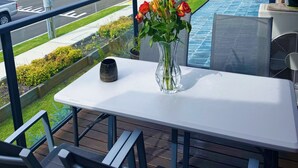 Uma varanda com uma mesa, um vaso de flores e vista para uma marina com barcos e uma estrada.