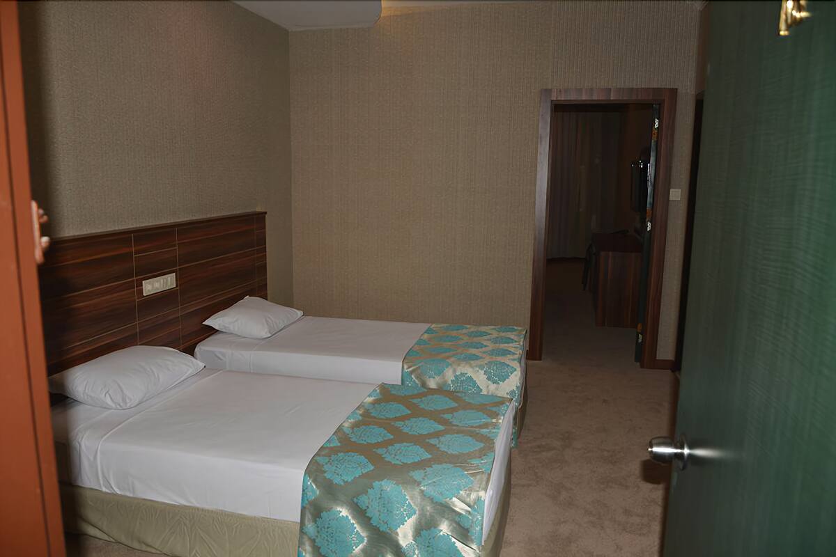 Quarto de hotel com duas camas, cabeceira de madeira e piso coberto por carpete.