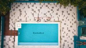 Vista aérea de uma piscina com duas pessoas mergulhando, cercada por um deck ladrilhado com o letreiro 'BaobaBed'.