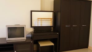 Quarto com escrivaninha de madeira escura, televisão e guarda-roupa.