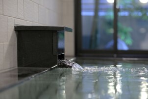 Canto de um quarto com um objeto preto, possivelmente um aquecedor, e uma superfície de vidro refletindo água.