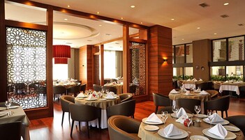 Um restaurante com mesas e cadeiras redondas, painéis de madeira e divisórias decorativas.