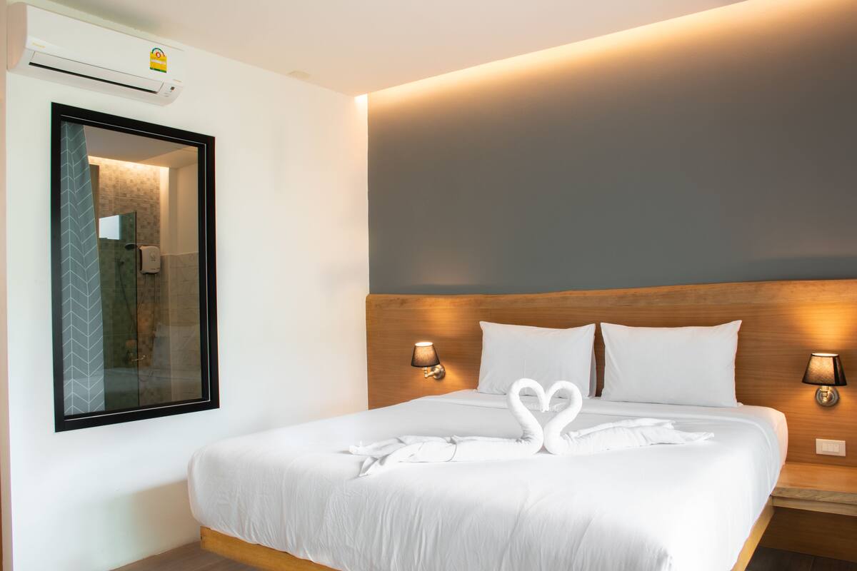 Cama bem arrumada com lençóis brancos e duas almofadas, cabeceira de madeira e duas luminárias fixadas na parede.