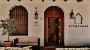 Entrada rústica de um edifício com porta de madeira, planta em vaso, sofá e banco de pedra.