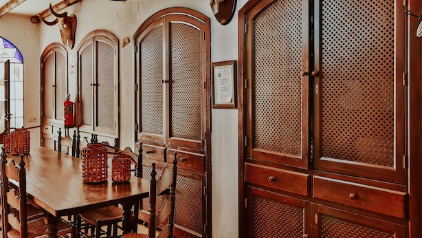 Uma zona de refeições tradicional em madeira, com uma grande mesa e cadeiras, portas de madeira arqueadas com painéis perfurados e um candeeiro pendente.