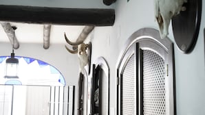 Quarto com teto rústico, uma janela grande com moldura azul e porta com grade de metal.
