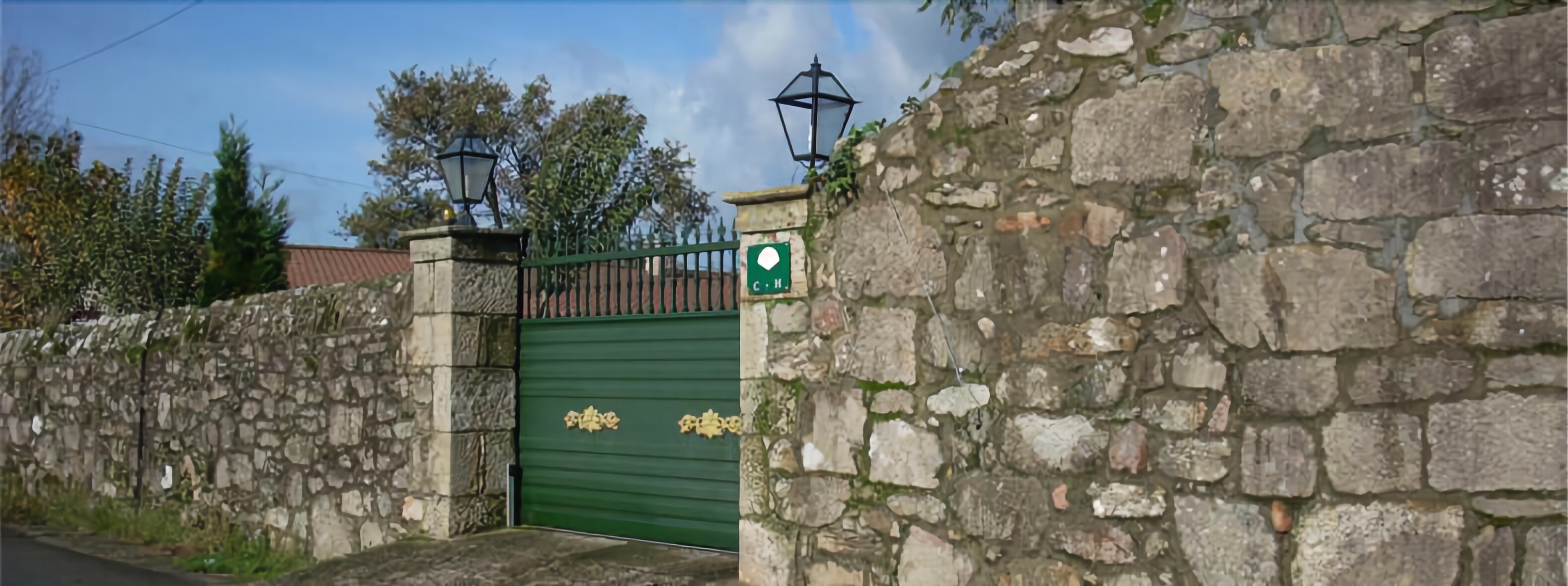 Um muro de pedra com um portão verde e uma placa com um símbolo branco.