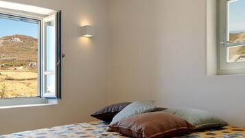 Quarto com uma janela ampla, cama com colcha estampada com girassóis e vista para uma paisagem montanhosa.