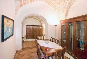 Uma sala de jantar com mesa e cadeiras de madeira, um armário de vidro com louças e um quadro na parede.