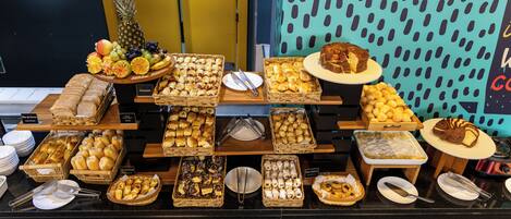 Buffet com diversos alimentos, incluindo pão, doces e frutas.