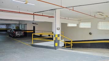 Garagem de estacionamento com barreira de segurança amarela, um carro e escadaria.